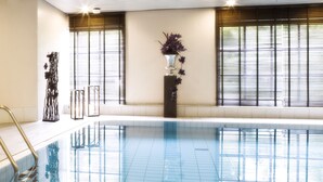 Piscina interna com água azul cristalina, grades de metal e elementos decorativos como um vaso com flores e obras de arte nas paredes.