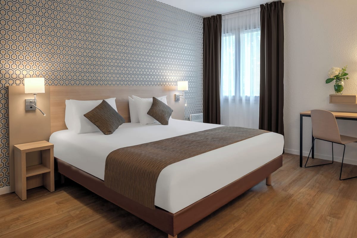 Quarto de hotel moderno com uma cama grande, mesas de cabeceira, escrivaninha e uma cadeira.