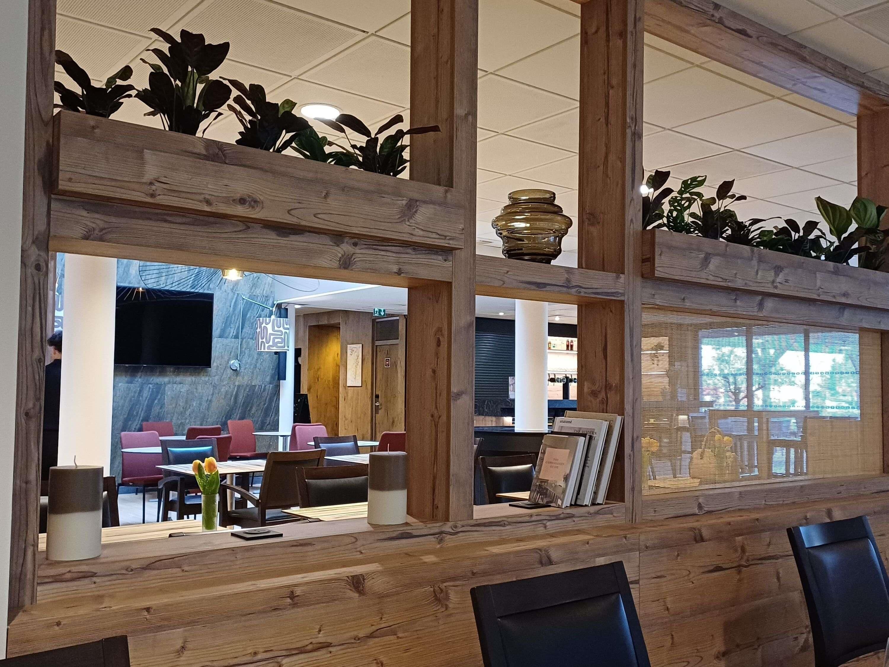 Um restaurante com vigas de madeira, plantas dentro e vista para a área de refeições.