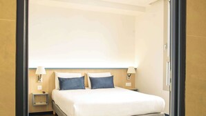 Quarto de hotel moderno com uma cama grande, duas mesas de cabeceira com abajures e piso coberto por carpete.