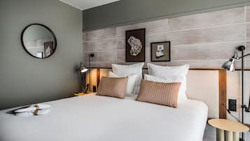 Cama bem arrumada com lençóis brancos e almofadas estampadas, um espelho redondo na parede e uma obra de arte emoldurada acima da cama.