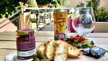 Disposição para piquenique com um pote de mostarda, uma lata de cerveja, um copo de vinho, pão e picles sobre uma mesa de madeira.