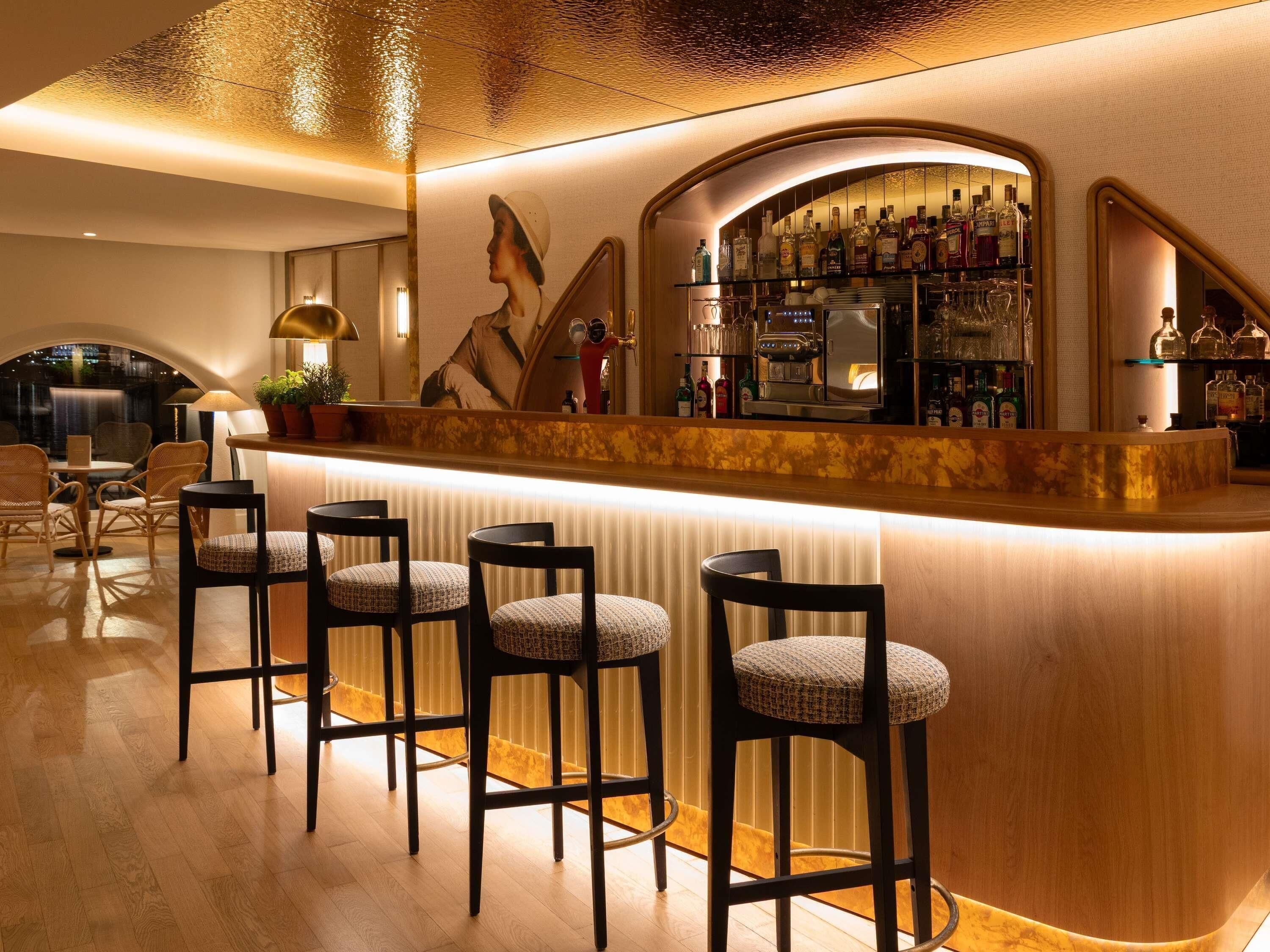 Uma área de bar com balcão curvo, banquetas e seleção de garrafas e copos.