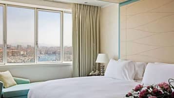 Quarto de hotel com uma cama grande, vista para a cidade, uma janela com cortinas e um vaso de flores.