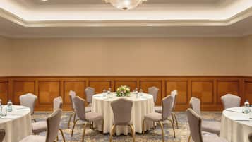 Uma sala de conferência com mesas redondas, cadeiras e um candelabro.