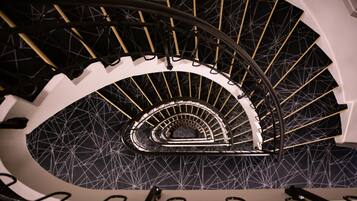 Uma escadaria em espiral com parede de padrão geométrico e guarda-corpo de metal.