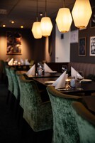 Restaurante com cadeiras estofadas em verde, mesas postas com guardanapos brancos, copos de vinho e uma vela sobre a mesa.