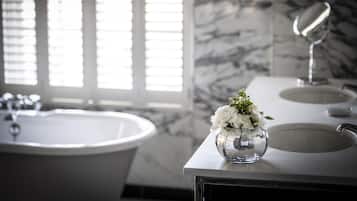 Um banheiro com banheira, duas pias, um espelho e um vaso de flores sobre o balcão.