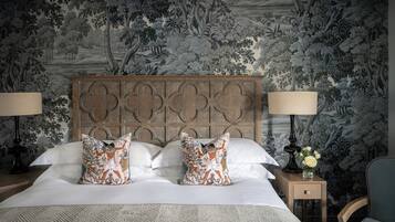 Quarto com cama grande, duas almofadas, mesa de cabeceira, abajur e uma cadeira.