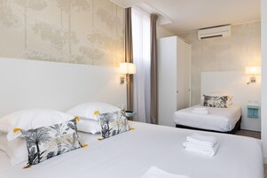 Quarto de hotel com duas camas, roupa de cama branca, um espelho grande e um ar condicionado fixado na parede.