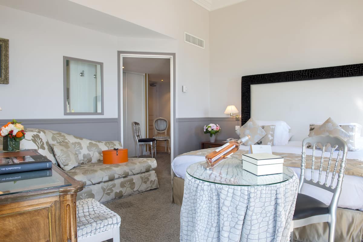 Quarto de hotel com sofá, mesa de vidro, cadeira, cama e espelho.