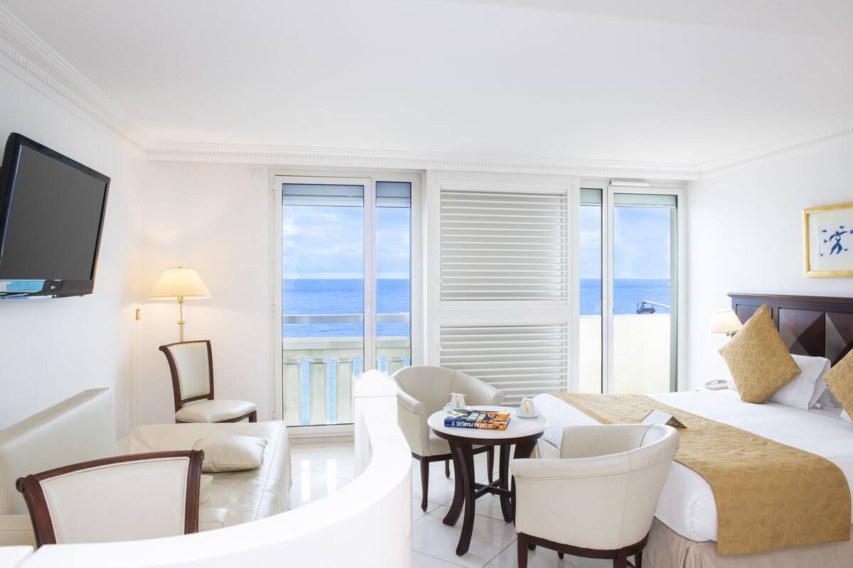 Quarto de hotel com varanda, cama, escrivaninha e televisão.