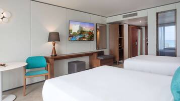 Quarto de hotel com duas camas, uma escrivaninha, uma cadeira, um abajur, uma televisão e um guarda-roupa.