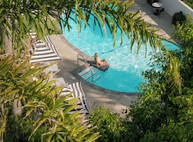 Uma área de piscina com espreguiçadeira, escada para piscina e vegetação ao redor.