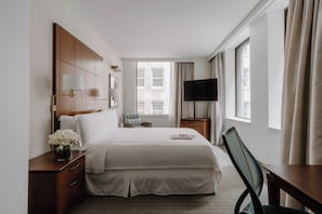 Quarto de hotel com uma cama grande, uma escrivaninha, uma cadeira, uma televisão e uma janela com cortinas.