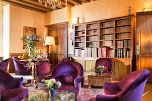 Uma biblioteca com estantes, um candelabro e poltronas roxas.