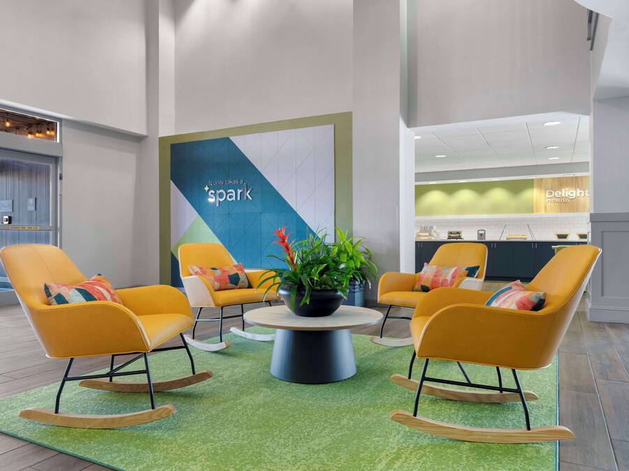 Um lobby moderno com poltronas de balanço amarelas, uma mesa de centro e um grande letreiro com a palavra 'spark'.