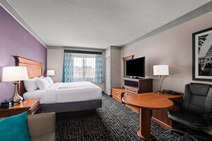 Quarto de hotel com cama, escrivaninha, televisão, cadeira e abajur.