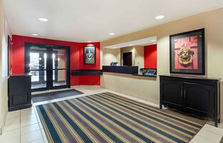 Um saguão de hotel com parede vermelha, balcão de recepção, armário preto e carpete listrado.