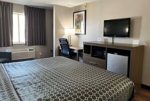 Quarto de hotel com cama, escrivaninha, cadeira, televisão e janela com cortinas.