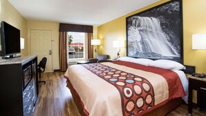 Quarto de hotel com cama, escrivaninha com televisão, cadeira, janela com cortinas e uma grande pintura de cachoeira na parede.