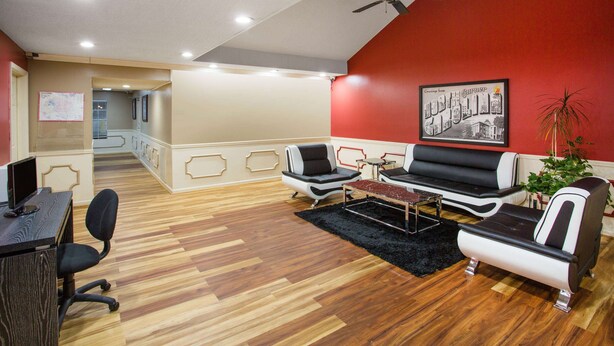Um espaço de escritório moderno com piso de madeira, uma mesa com computador, dois sofás preto e branco, um ventilador de teto e um quadro na parede.
