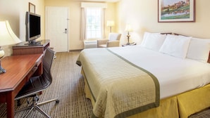 Quarto de hotel com cama, escrivaninha, cadeira, televisão e luminárias.