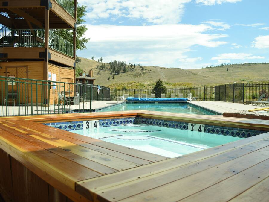 Área de hidromassagem com deck de madeira, piscina e vista para uma paisagem montanhosa.