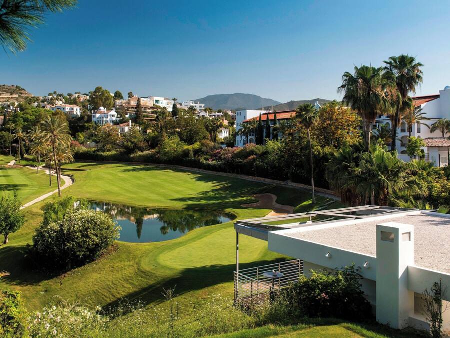 Um campo de golfe com lago, rodeado por vegetação exuberante e palmeiras.