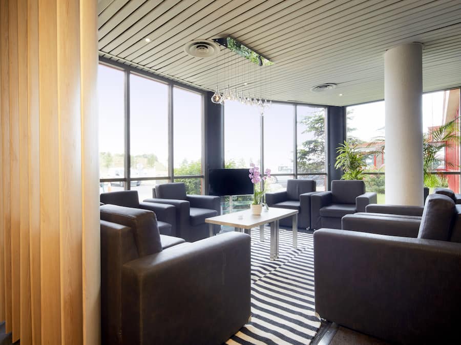 Uma área de estar moderna com sofás, uma mesa de centro e uma TV de tela plana. Janelas amplas proporcionam luz natural e vistas para o exterior.