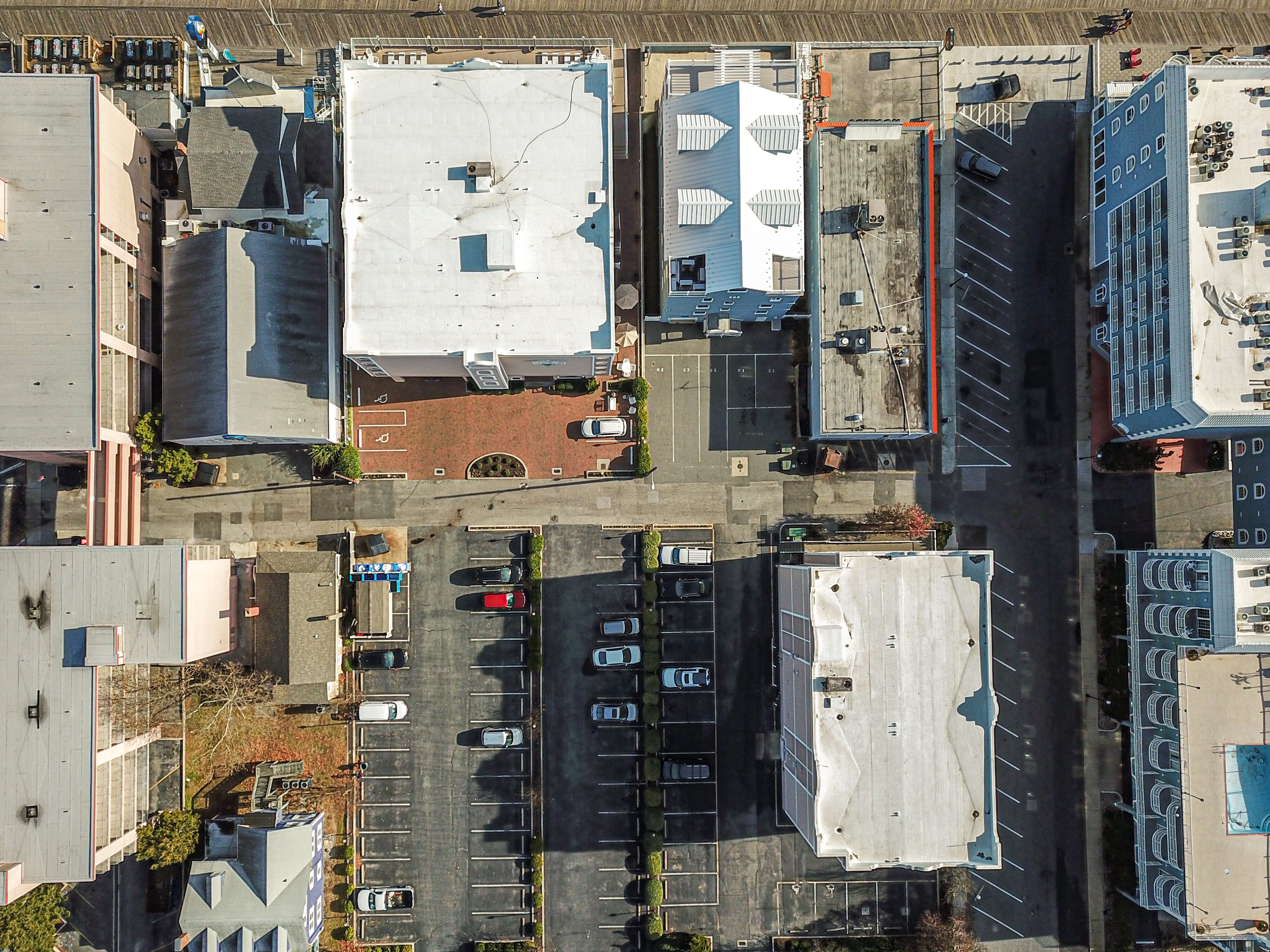 Vista aérea de um estacionamento com várias fileiras de carros estacionados, cercado por edifícios com telhados planos e janelas grandes.