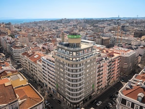 Um edifício alto com várias varandas, uma placa verde chamativa e vista para a paisagem urbana ao redor.