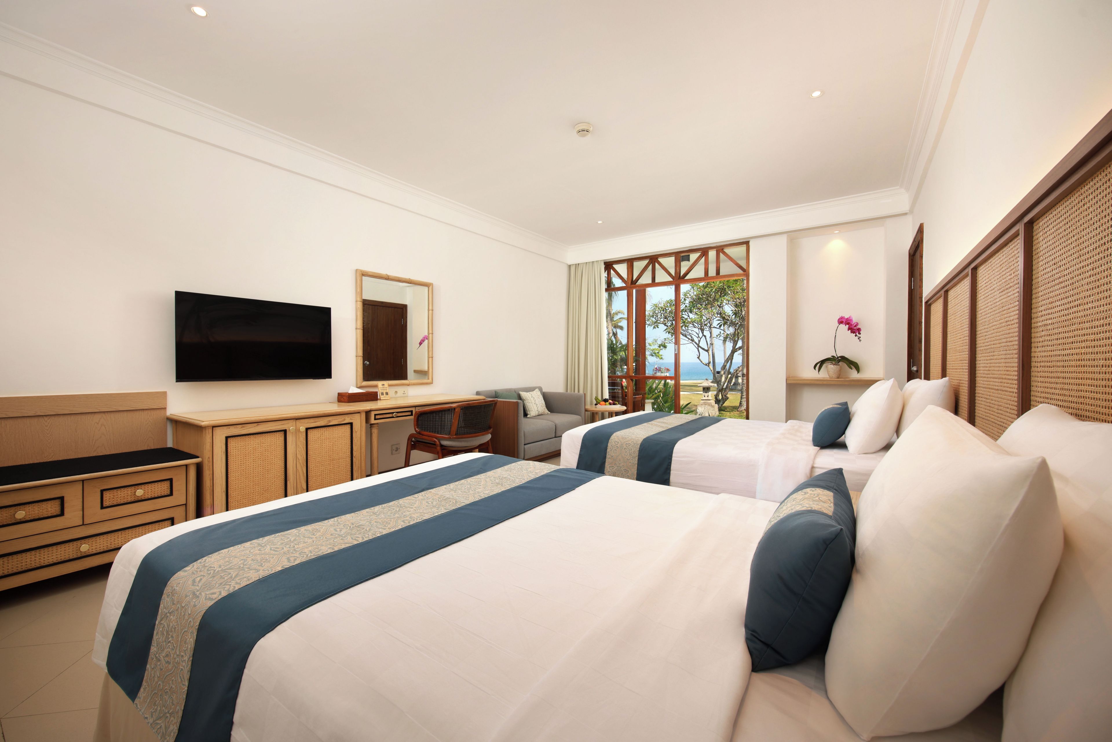 Quarto de hotel com duas camas, televisão, escrivaninha e vista para o exterior.