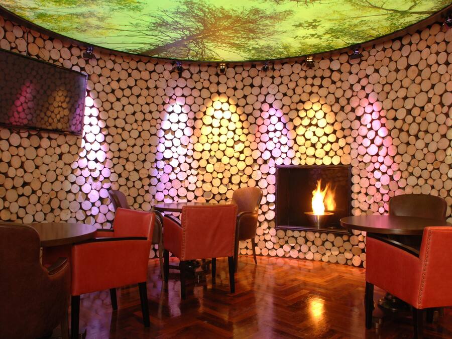 Um restaurante com uma parede de lenha empilhada, lareira e cadeiras estofadas vermelhas.