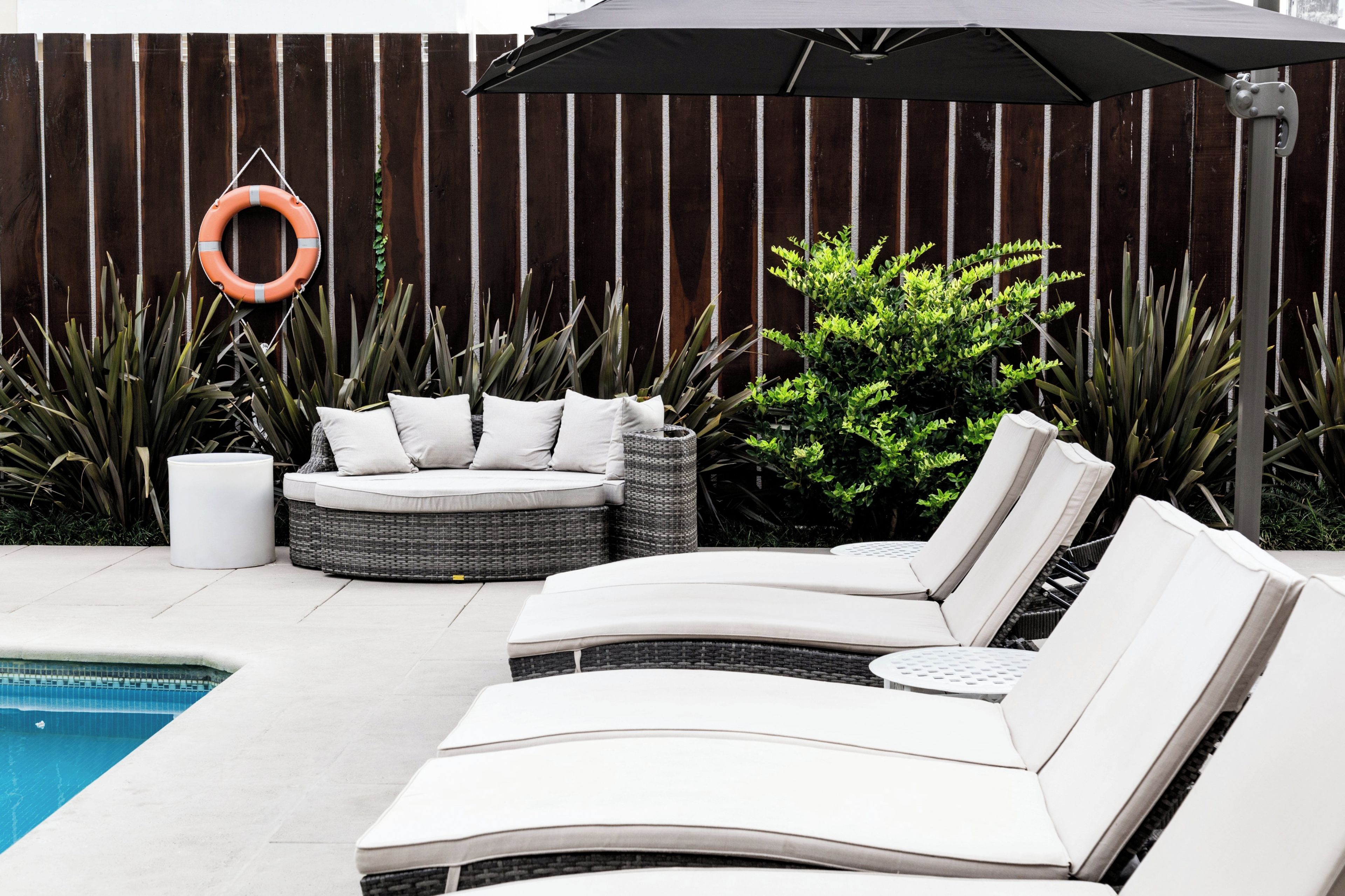 Uma área de piscina com duas espreguiçadeiras, um espaço de estar circular e um flutuador preso a uma cerca de madeira.