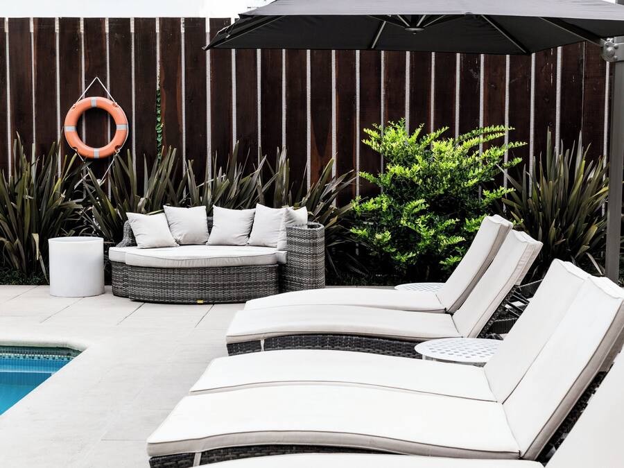 Uma área de piscina com duas espreguiçadeiras, um espaço de estar circular e um flutuador preso a uma cerca de madeira.