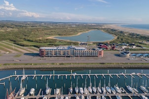 Marina com vários barcos atracados, um edifício grande com telhado característico e vista da paisagem circundante, incluindo um corpo de água e terra ao longe.