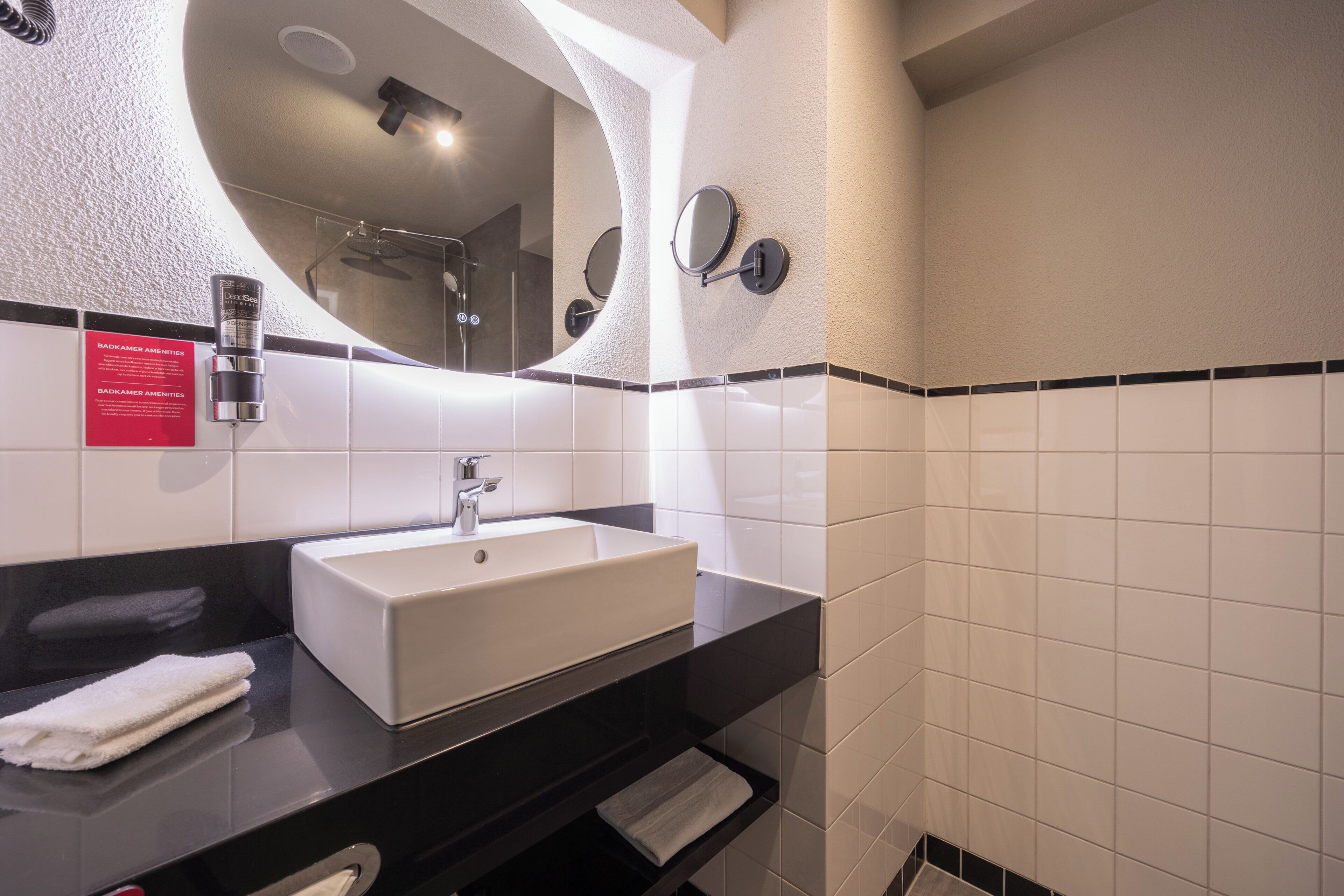 Casa de banho moderna com lavatório branco, bancada preta e um espelho grande.