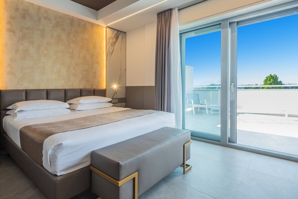 Quarto de hotel moderno com uma cama grande, uma mesa de cabeceira e vista para o exterior.