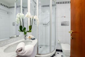 Um banheiro moderno com chuveiro em cabine de vidro, pia de mármore e vaso sanitário.