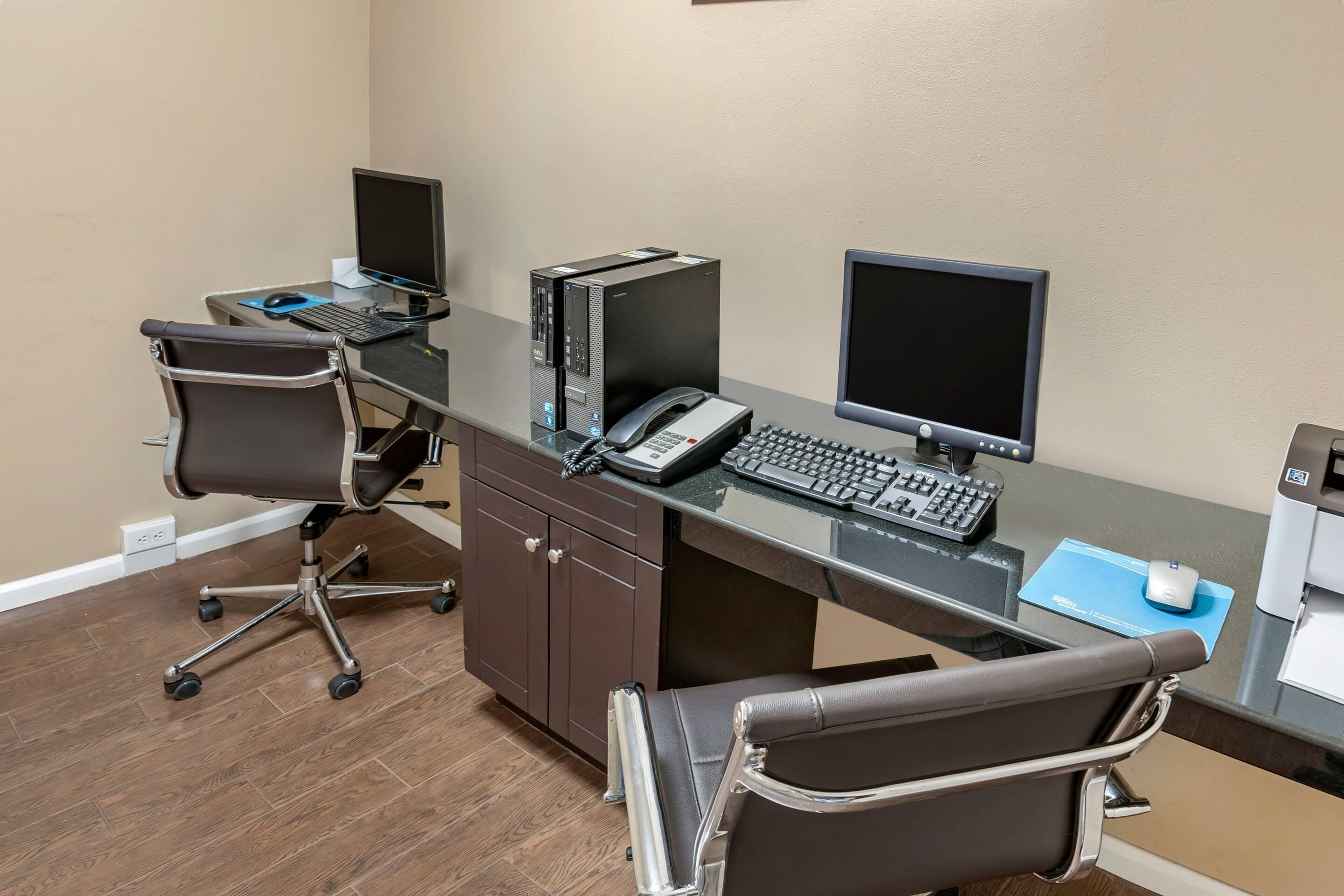 Um escritório moderno com escrivaninha de vidro, duas cadeiras de escritório, um computador de mesa, monitor, telefone e impressora.