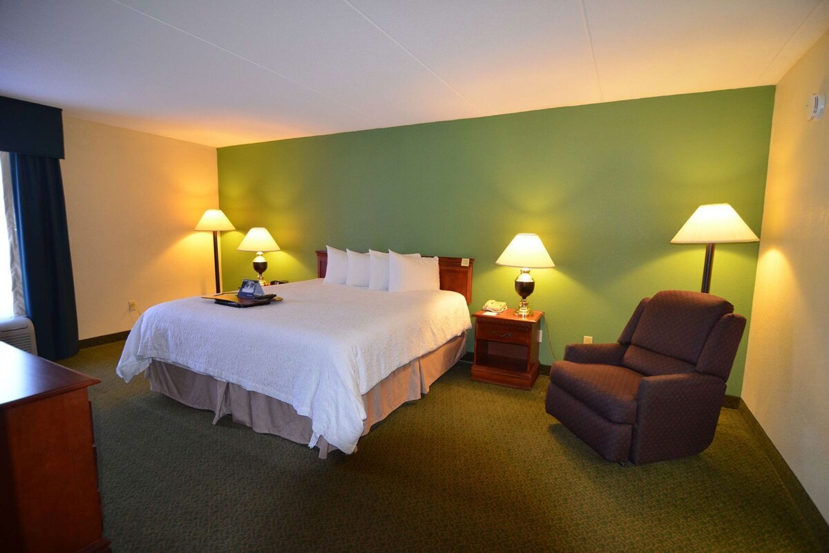Quarto de hotel com uma cama, duas mesas de cabeceira, uma cadeira e uma escrivaninha.
