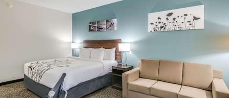 Quarto de hotel com cama, mesa de cabeceira, abajur e sofá.