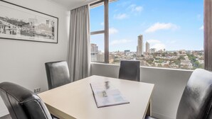 Uma sala de conferências com uma mesa e quatro cadeiras, uma fotografia emoldurada da paisagem urbana na parede e vista da cidade através de grandes janelas.