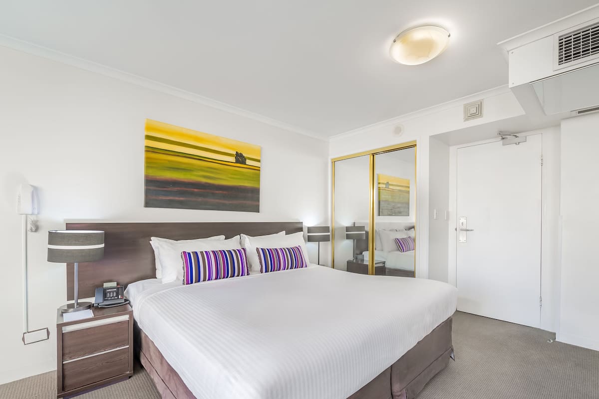 Quarto de hotel moderno com uma cama grande, mesas de cabeceira, um espelho e um quadro na parede.