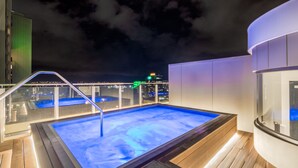 Piscina no terraço com barreira de vidro, deck de madeira e paisagem urbana ao fundo.