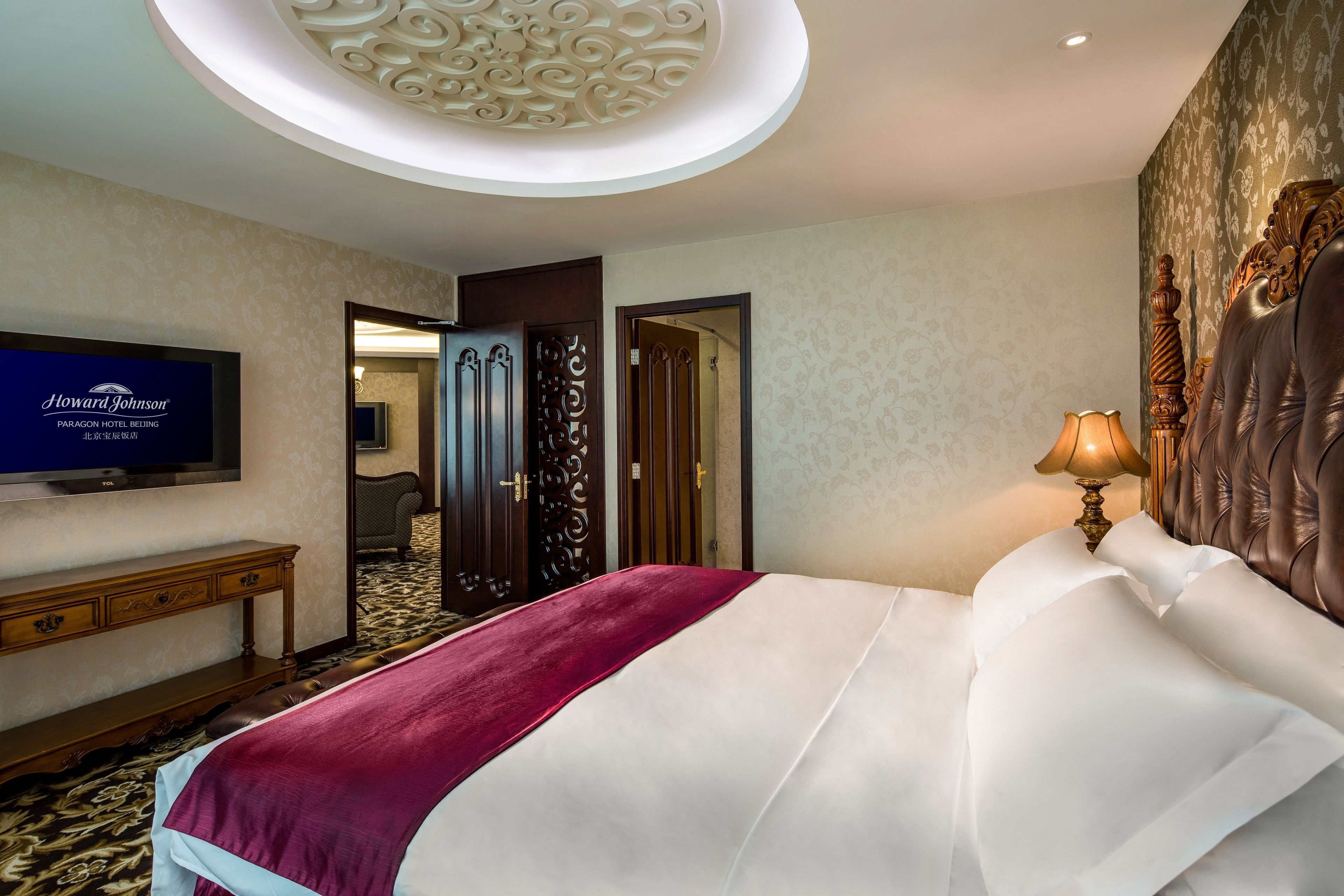 Quarto de hotel com uma cama grande, televisão na parede e luminária no teto.