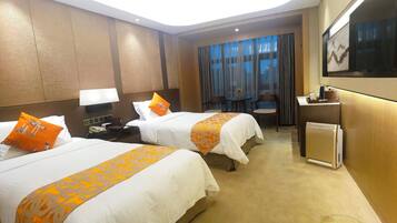 Quarto de hotel com duas camas, uma escrivaninha, uma cadeira, uma mesinha, uma televisão e uma janela com cortinas.