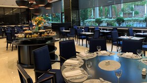 Uma sala de jantar moderna com mesas redondas, cadeiras azuis e um buffet central.