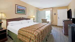 Quarto de hotel com cama, televisão, escrivaninha com abajur, cadeira e porta para outro cômodo.